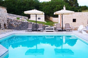 Uma piscina com espreguiçadeiras e guarda-sóis, rodeada por paredes de pedra e vegetação.
