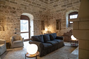 Um quarto com paredes de pedra, um sofá, poltronas e uma mesa com abajur.