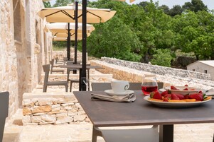 Um café ao ar livre com paredes de pedra, mesas e guarda-sóis.