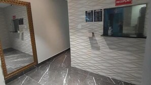 Uma área de recepção com balcão, espelho e piso em azulejos.