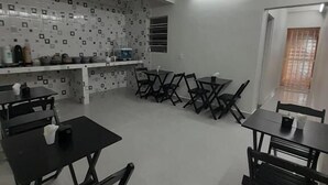 Uma área de refeições com mesas e cadeiras, uma cozinha com painel decorativo e uma janela com cortinas.