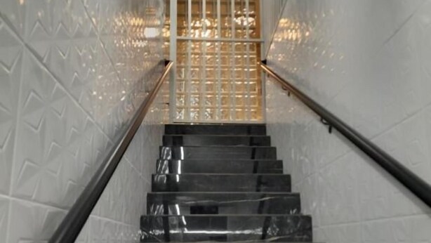 Uma escadaria com degraus de mármore preto, paredes brancas e corrimão de metal.