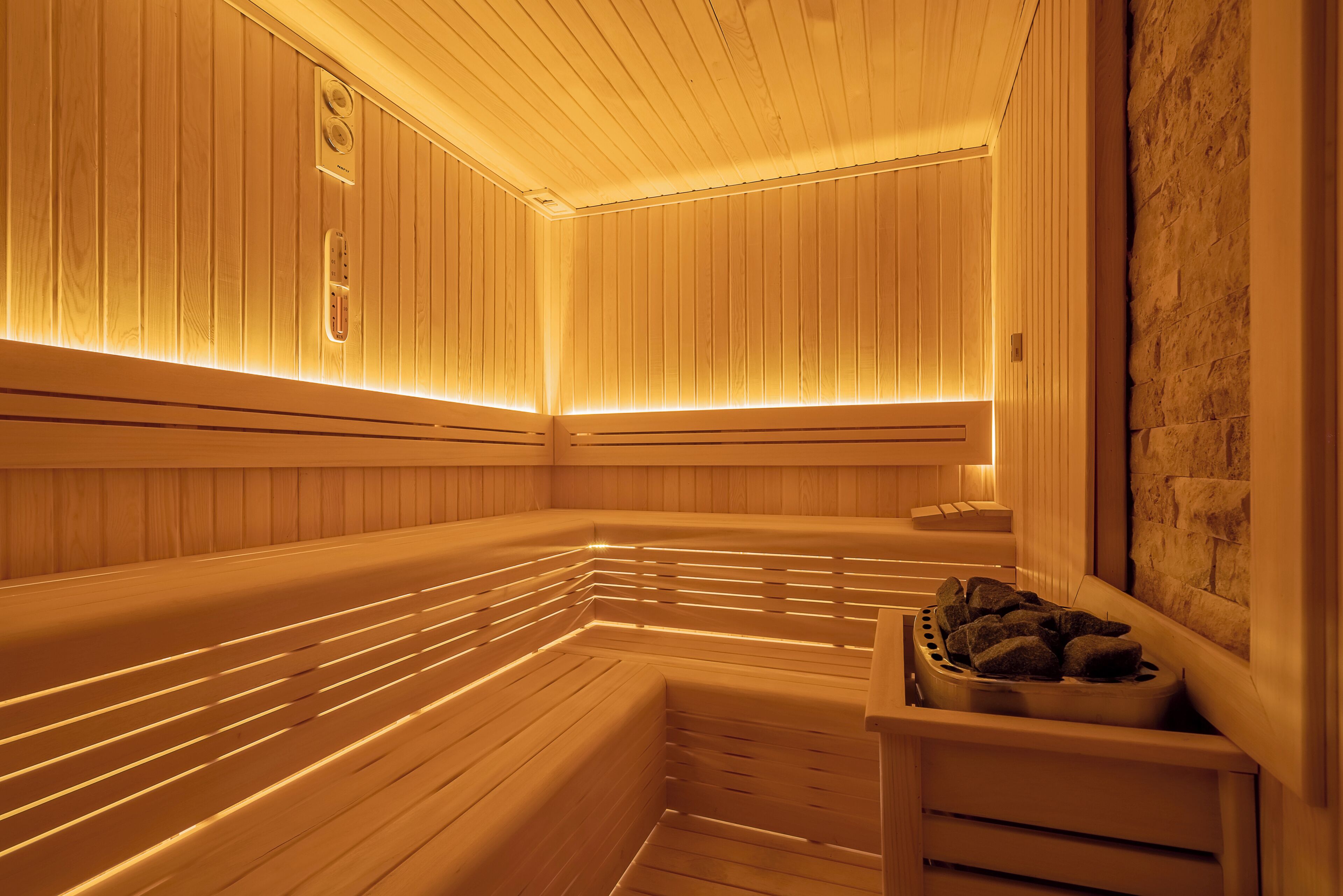 Uma sauna com painéis de madeira e bancos, um painel de controle e uma parede de pedra.