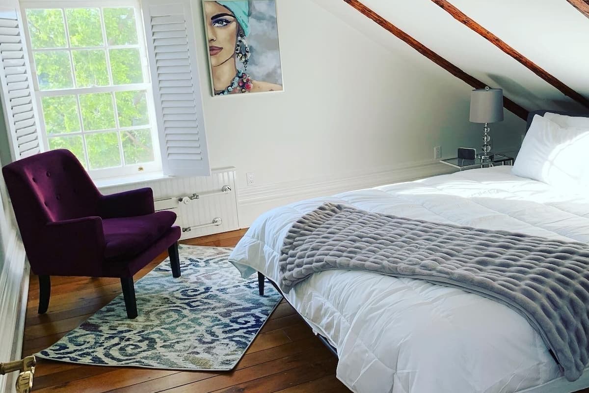 Um quarto com uma cama, uma cadeira, um quadro e uma janela.