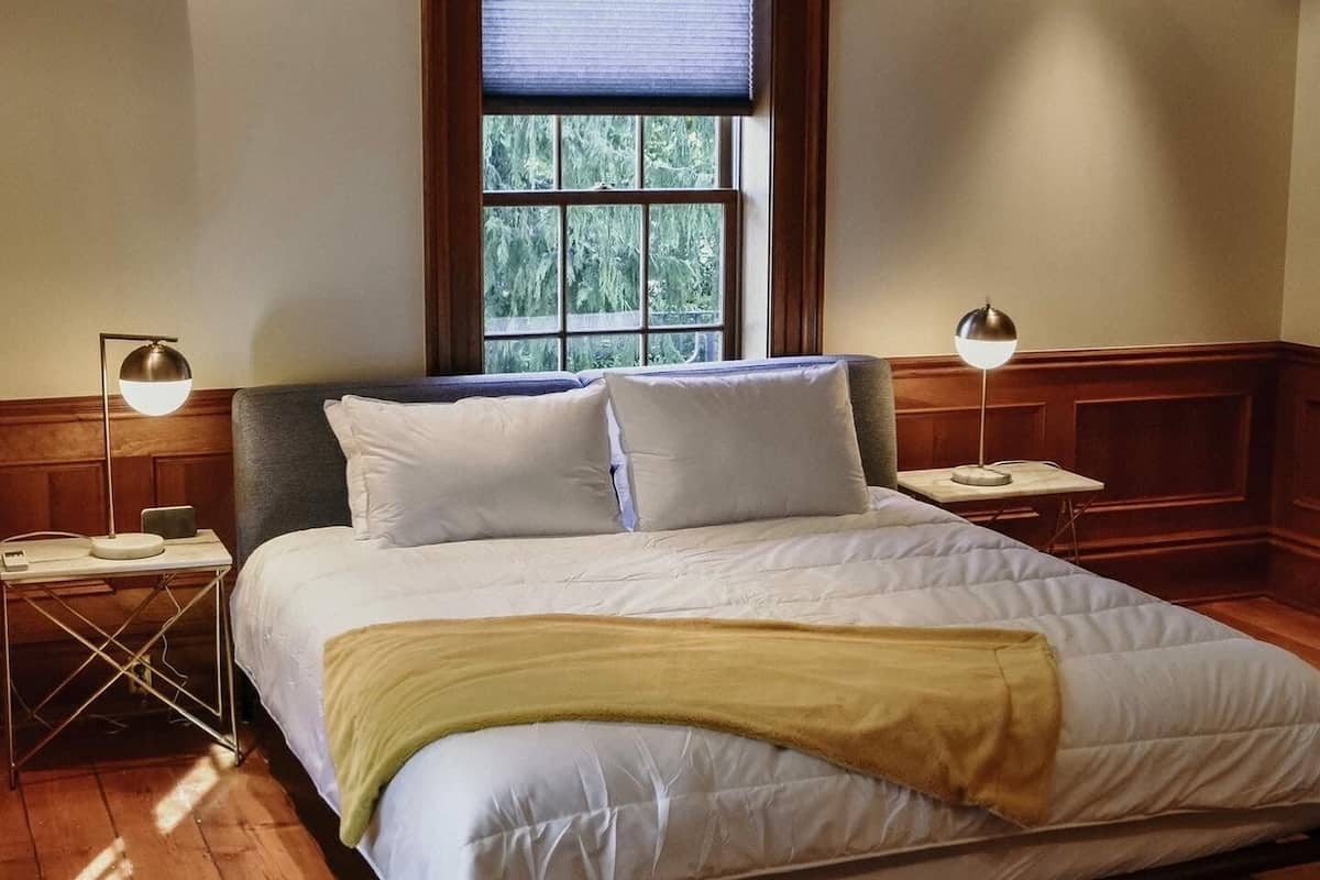 Um quarto com uma cama, janela, mesa de cabeceira e luminária.