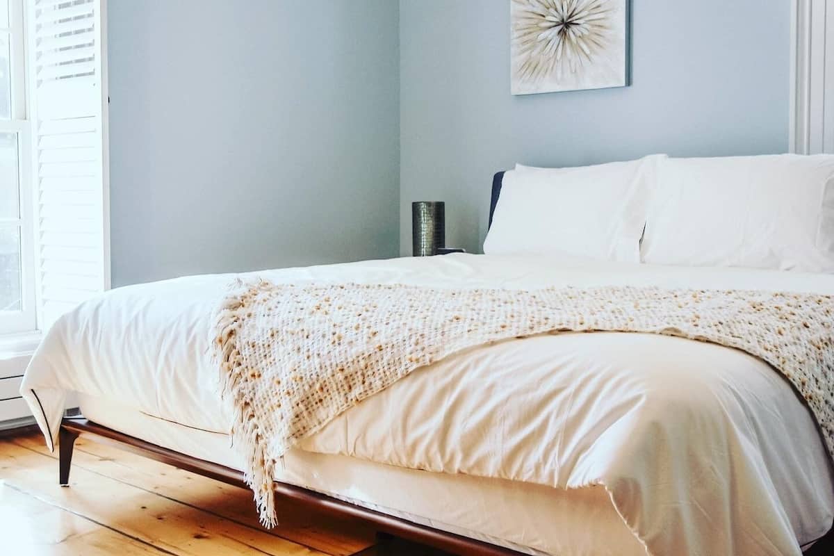 Quarto com cama, janela com persianas e uma obra de arte pendurada na parede.