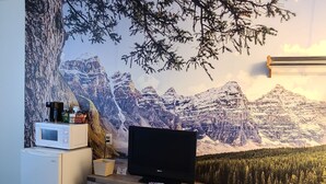 Quarto com um mural de montanhas, uma TV sobre um suporte de madeira, um mini-refrigerador e uma cama.