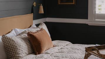 Uma cama com roupa de cama xadrez, um travesseiro marrom e uma cesta de fibra.