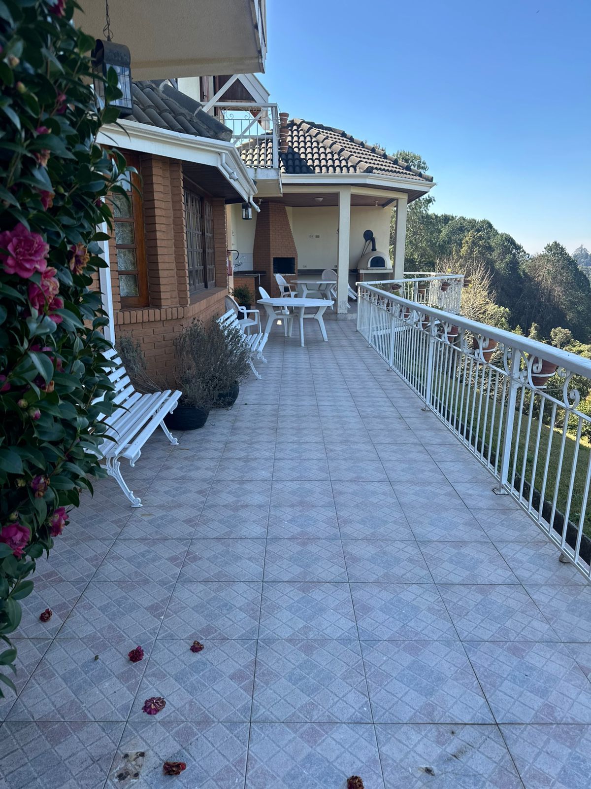 Uma varanda com piso de azulejos, móveis brancos e corrimão branco.