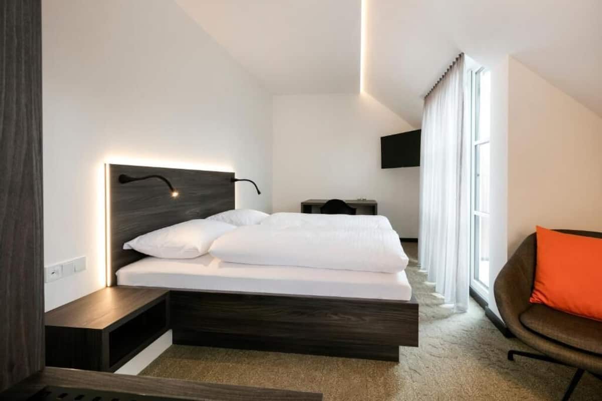 Quarto moderno com cama, mesas de cabeceira, televisão e janela com cortinas.