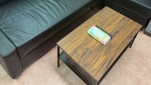 Uma sala de estar moderna com um sofá de couro preto, uma mesa de centro de madeira e uma janela com cortinas claras.