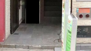Entrada de um edifício com chão de azulejos e escadaria. Placas com texto e números à direita.
