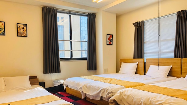 Quarto de hotel com duas camas, um tapete xadrez vermelho e preto, e uma janela com cortinas.