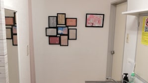Um corredor estreito com uma pia e um espelho à direita, uma porta no final e uma parede com quadros.