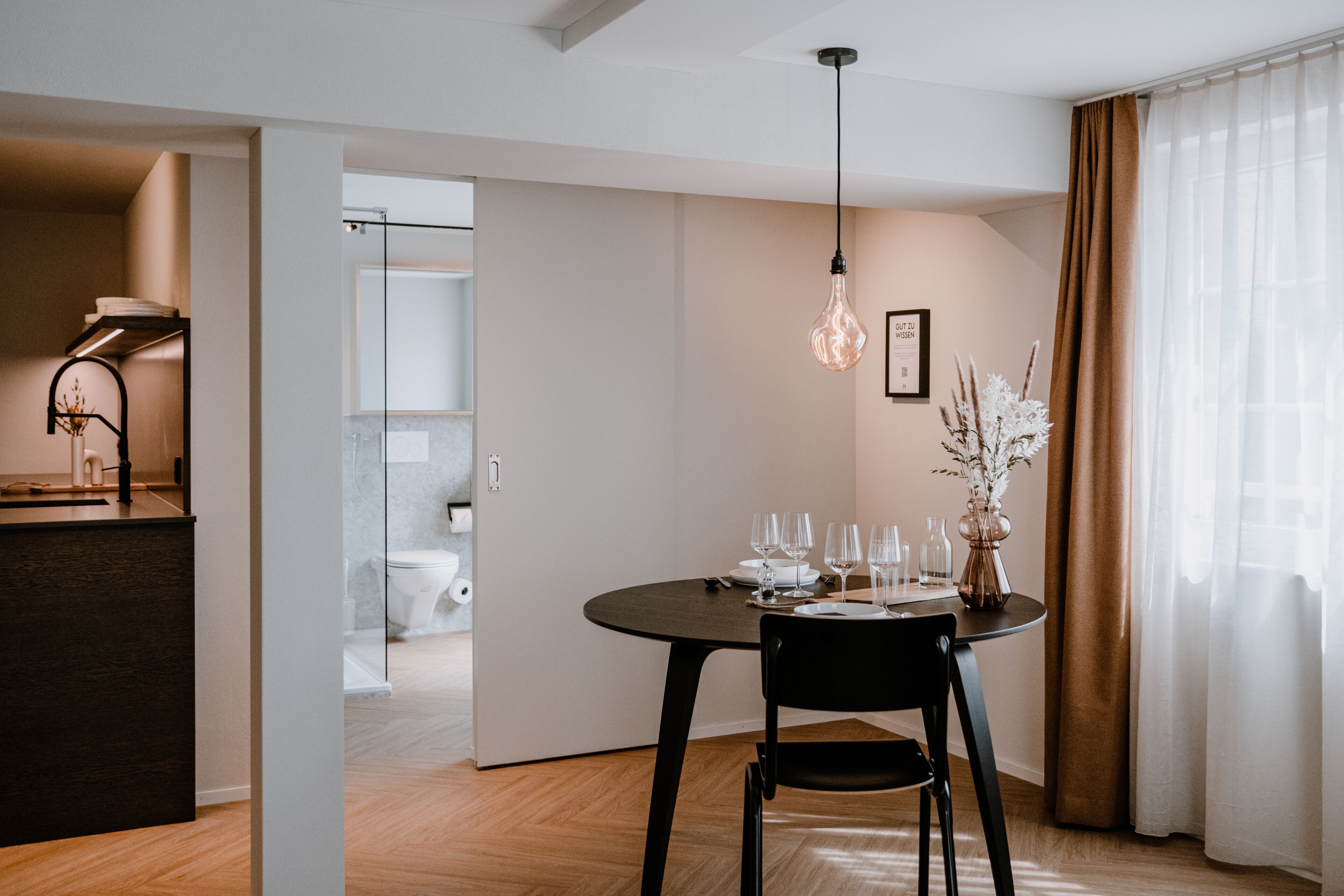 Uma sala de jantar moderna com uma mesa redonda, cadeiras pretas e um lustre.