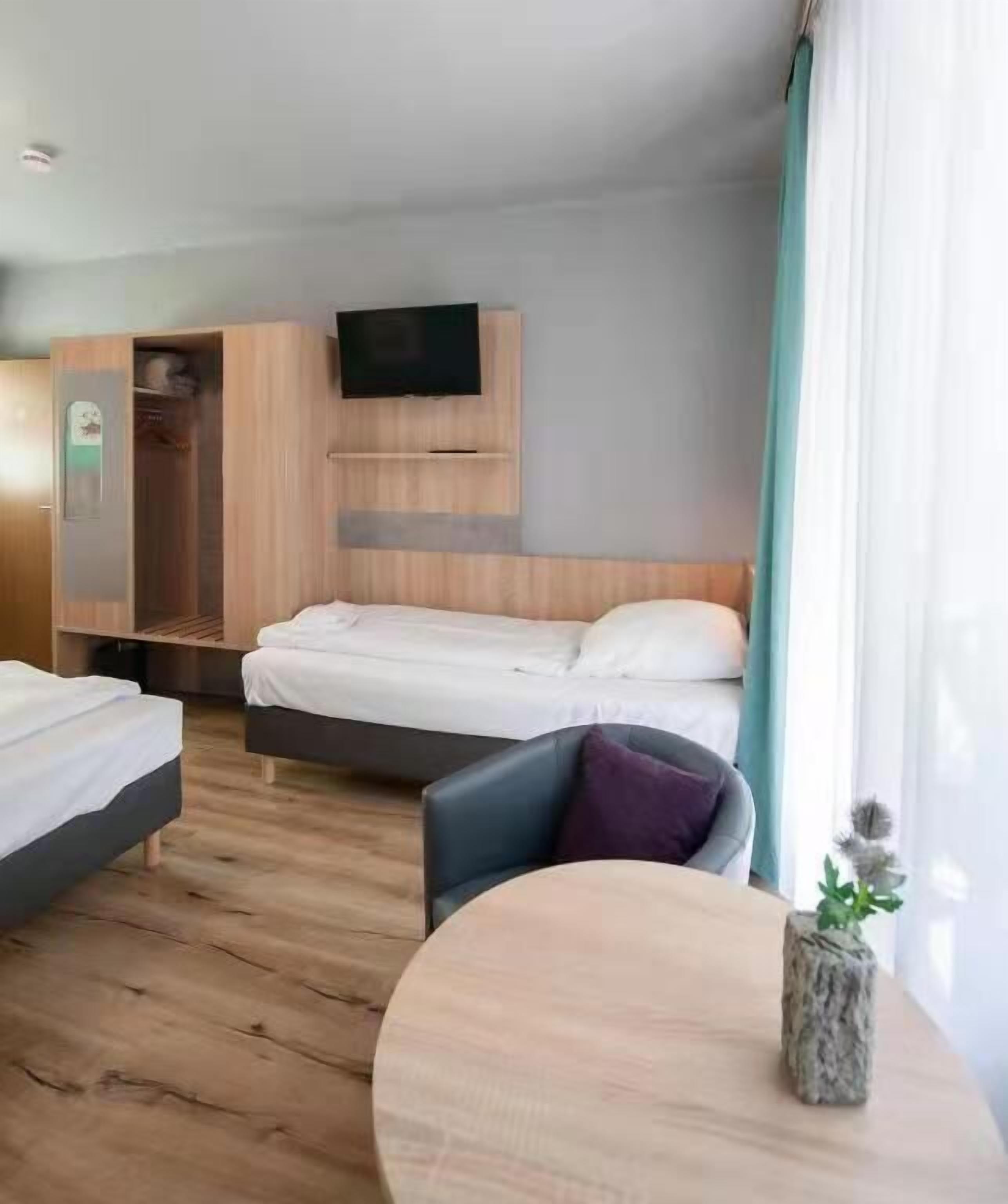 Quarto de hotel com duas camas, televisão na parede, guarda-roupa e uma pequena mesa redonda com um vaso.