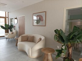 Uma sala de estar moderna com um sofá curvo, uma pequena mesa redonda de madeira e grandes vasos de plantas.