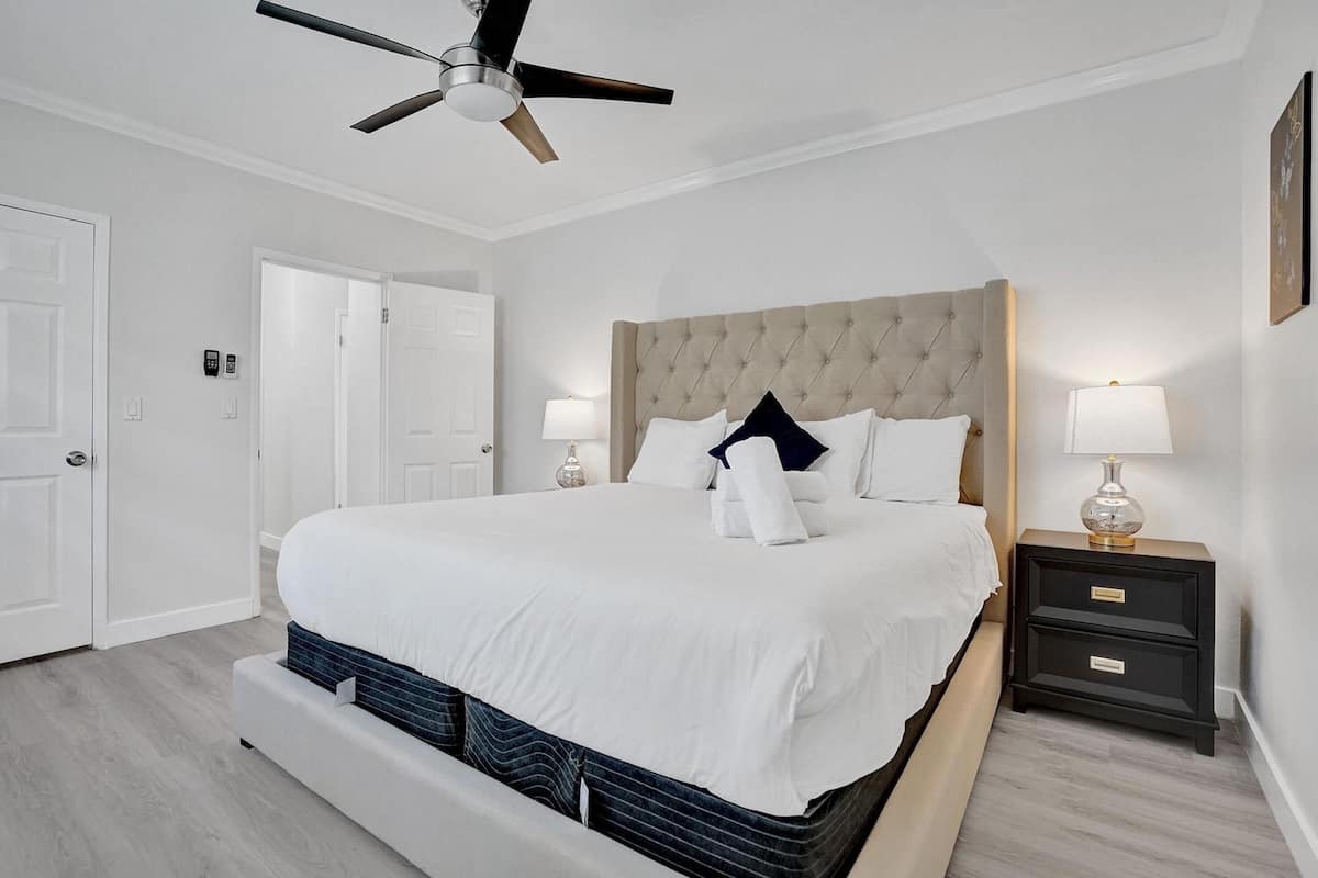 Quarto bem organizado com uma cama grande, uma mesa de cabeceira com abajur e um ventilador de teto.