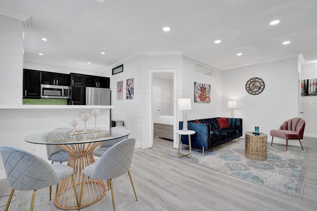 Uma sala de estar moderna com uma mesa de jantar de vidro, um sofá azul e uma poltrona rosa.
