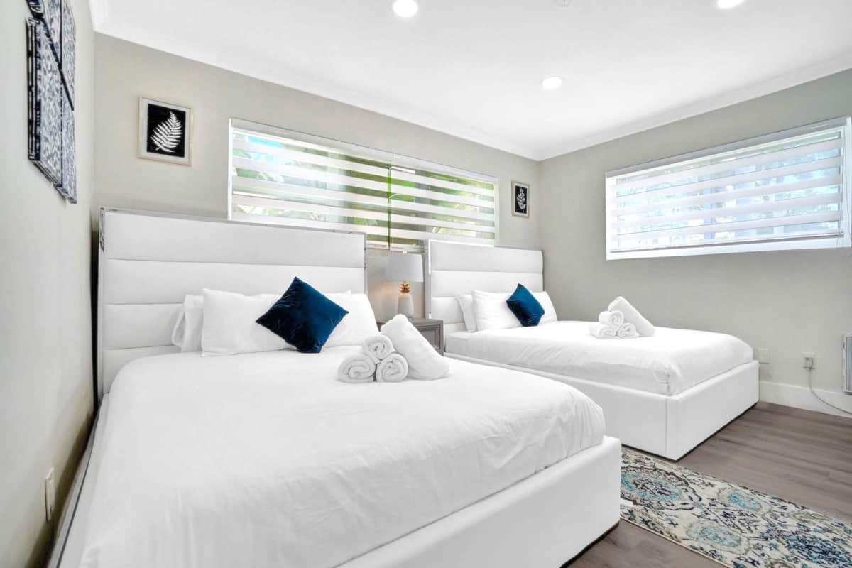 Quarto de hotel com duas camas, roupa de cama branca e tapete estampado.