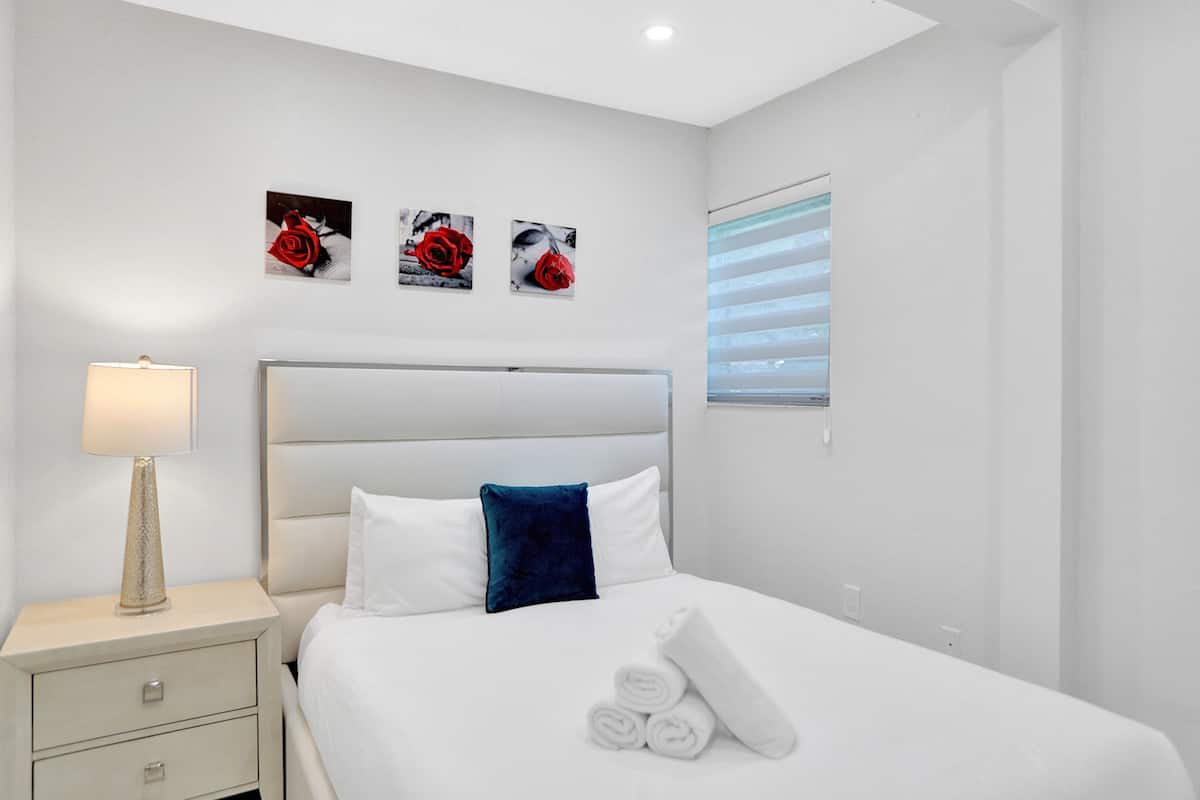 Quarto de hotel com uma cama, mesa de cabeceira, abajur e três quadros na parede.