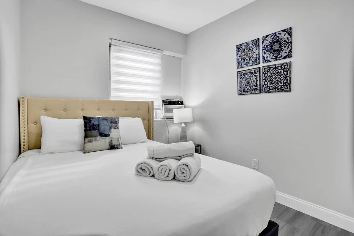 Uma cama bem arrumada com toalhas enroladas, um abajur e uma parede com quatro azulejos estampados.