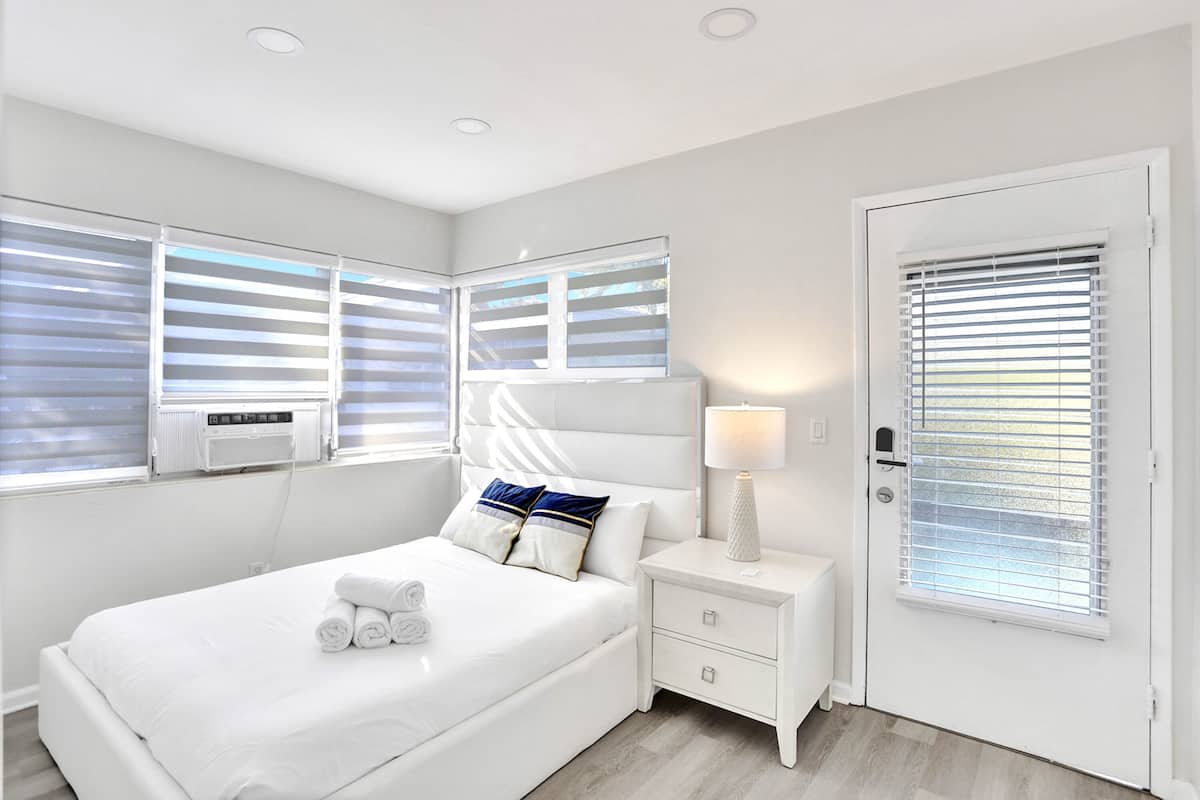 Quarto moderno com cama grande, mesas de cabeceira e porta com persianas.