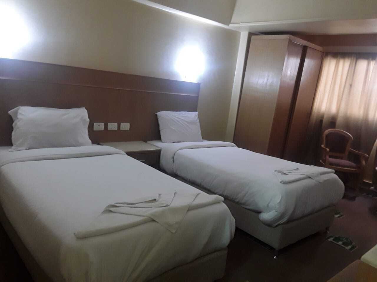 Quarto de hotel com duas camas, mesa de cabeceira, cadeira e guarda-roupa.