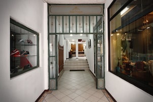 Entrada de hotel com chão de azulejos, escada de madeira e porta de vidro com moldura metálica.