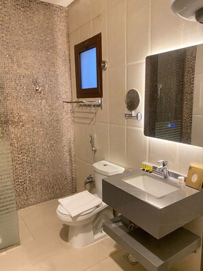 Um banheiro moderno com parede em mosaico, vaso sanitário embutido, toucador com espelho e área de chuveiro.
