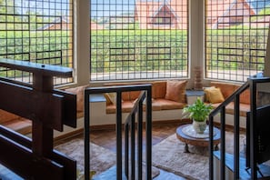 Uma área de estar acolhedora com um sofá e uma mesa pequena, uma escada com corrimão e vista pela janela com padrão quadriculado.