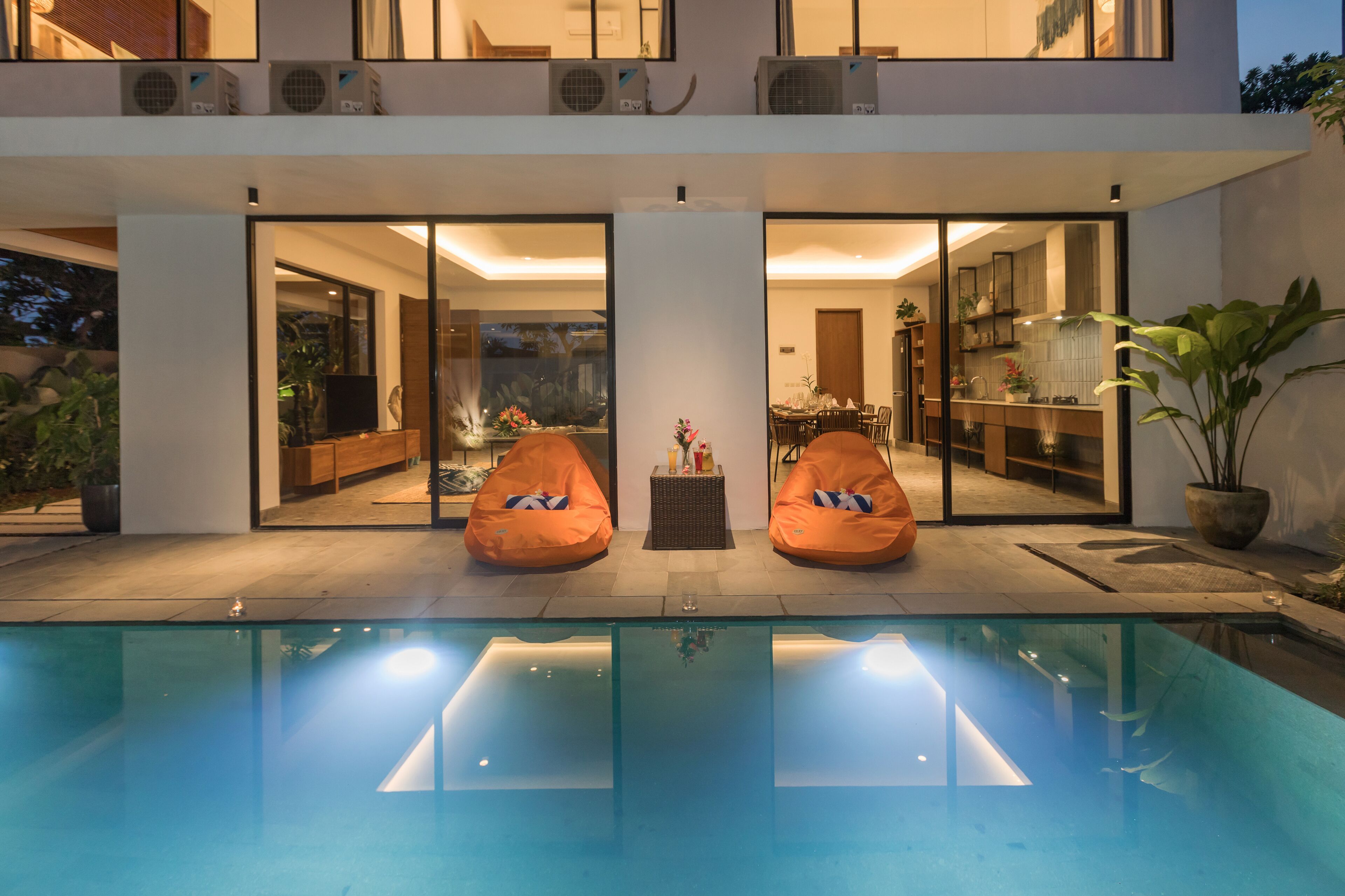Uma casa moderna com piscina, dois bean bags e uma área de refeições visível através de portas de vidro.