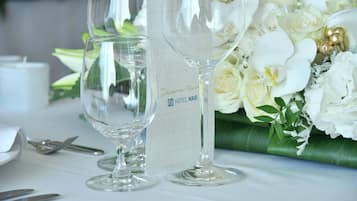 Uma mesa posta com copos de vidro transparente, um cardápio e um arranjo floral.