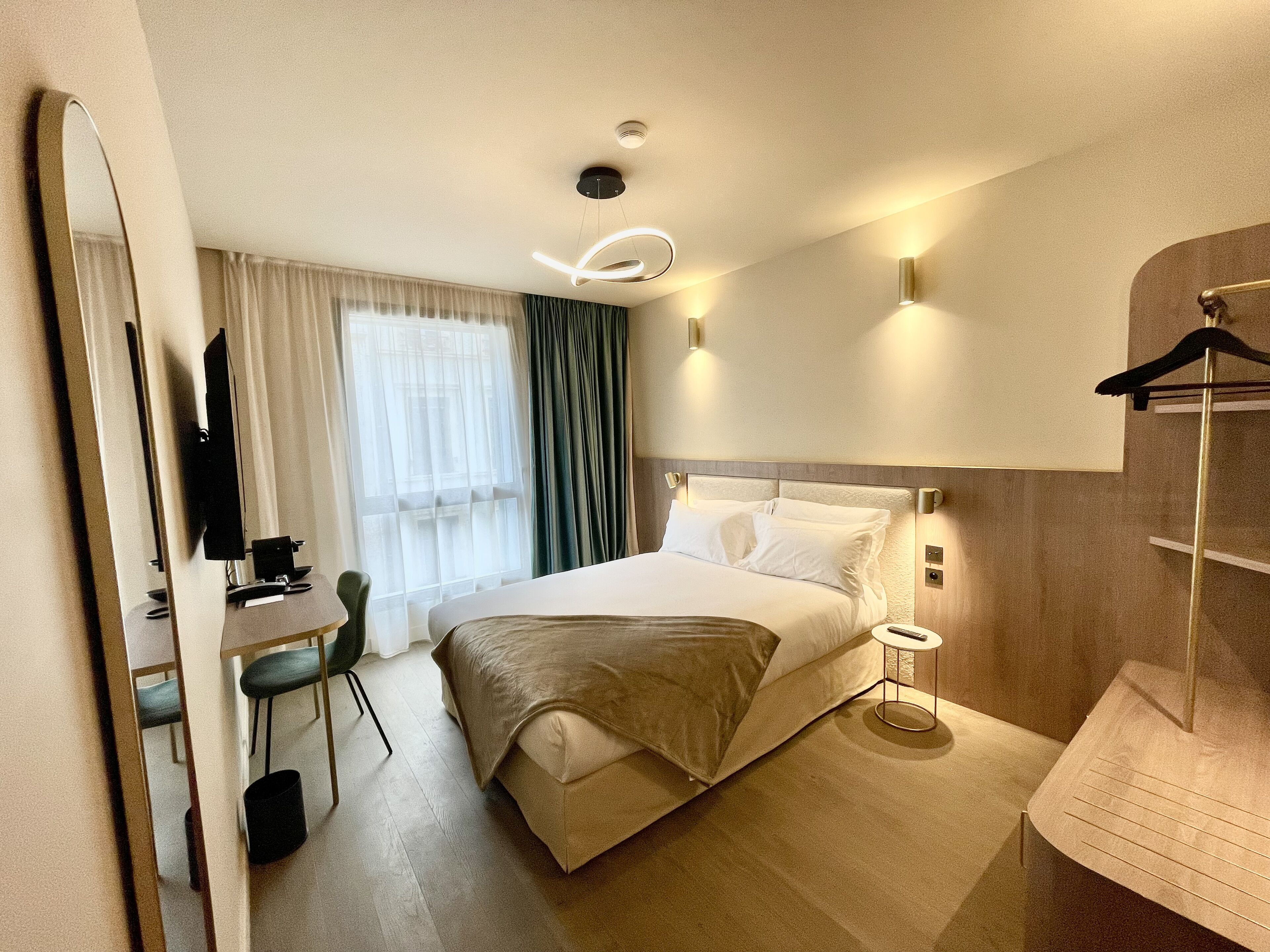 Quarto de hotel moderno com cama grande, mesa de cabeceira e espelho.