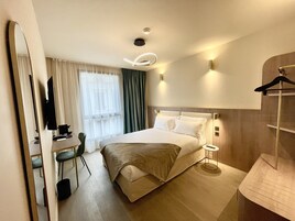 Quarto de hotel moderno com cama grande, mesa de cabeceira e espelho.
