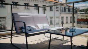 Uma varanda com um sofá branco e uma mesa de vidro, com vista para a cidade.