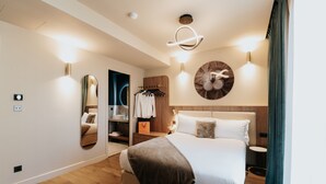 Quarto de hotel moderno com uma cama grande, mesas de cabeceira, um espelho, luminárias fixadas na parede e cabeceira de madeira.