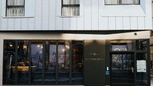 Entrada de um hotel com fachada de vidro, porta preta e uma placa com a inscrição "Keystone Hotel".