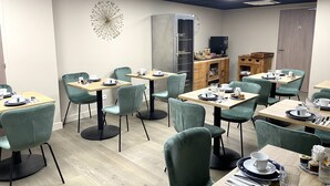 Uma área de refeições com várias mesas e cadeiras, equipada com pratos, copos e talheres.