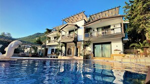 Um edifício de dois andares com varandas, piscina e montanhas ao fundo.