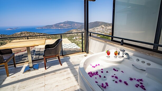 Varanda com vista para o mar, banheira de hidromassagem com pétalas de rosa e mesa com cadeiras.