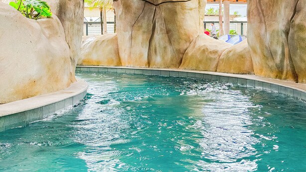 Uma piscina com águas turquesa cristalinas, rodeada por grandes formações rochosas e palmeiras.