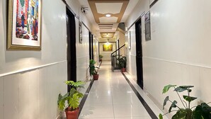 Corredor de hotel com piso de azulejos, plantas em vasos, quadros e escada no final.