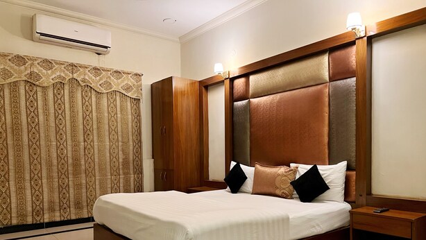 Quarto de hotel com uma cama grande, cabeceira de madeira e mesa de cabeceira com caixa de lenços.