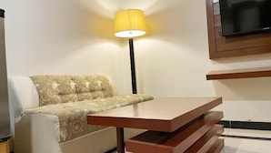 Uma sala de estar com um sofá, uma mesa de centro de madeira, um abajur e uma televisão de tela plana fixada na parede.