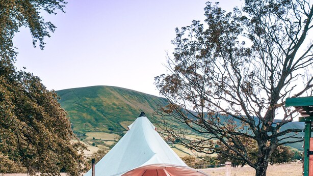 Uma tenda montada numa área gramada, com vista para colinas ao fundo.