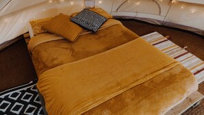 Um quarto em estilo de tenda aconchegante e bem iluminado, com cama, almofadas e cobertor.