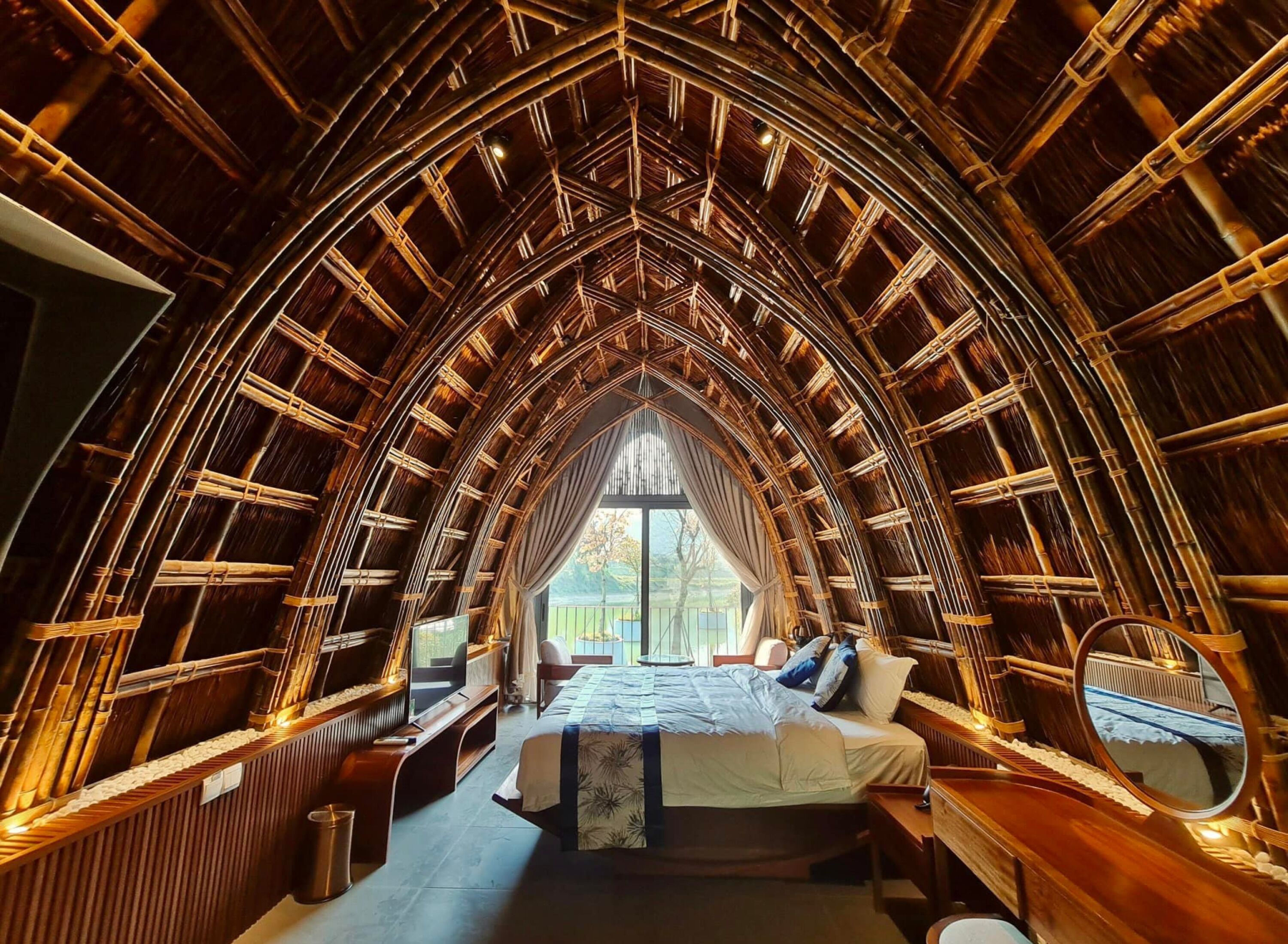 Um quarto com teto abobadado, uma cama com almofadas, uma mesa de cabeceira e uma janela com vista.