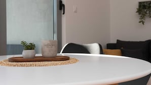 Uma sala de jantar moderna com uma mesa branca, um tabuleiro de madeira, uma planta em vaso e um castiçal.