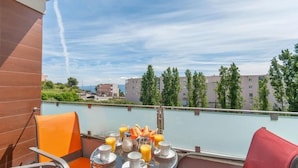 Varanda com mesa posta para café da manhã, com vista para um corpo de água e edifícios.
